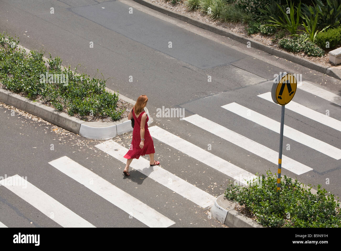 Ginger haired lady in red summer dress walking across a zebra pelican ...