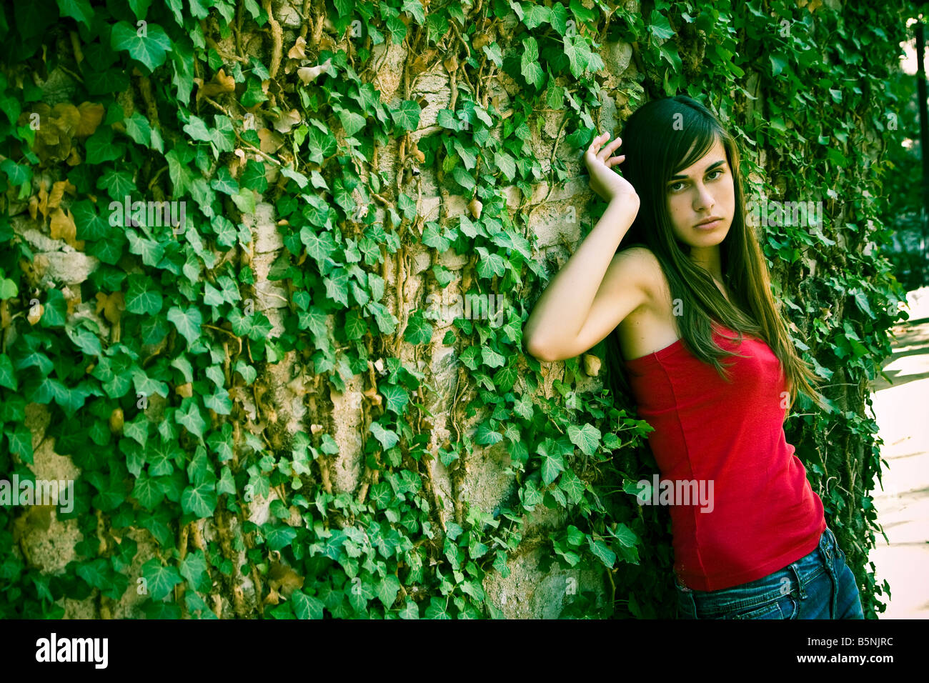 Young woman on wall full of leaves Stock Photo - Alamy