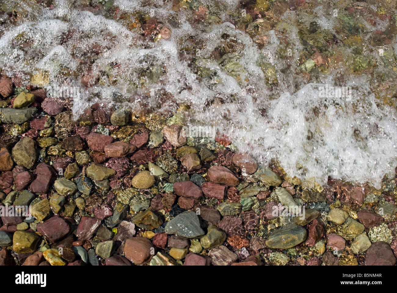 Waves more across colorful pebbles along the shores of lake McDonald ...