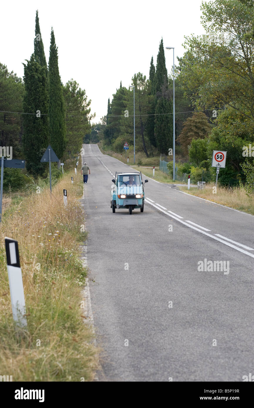A blue Italian Ape three wheeled utility vehicle approaches along a ...
