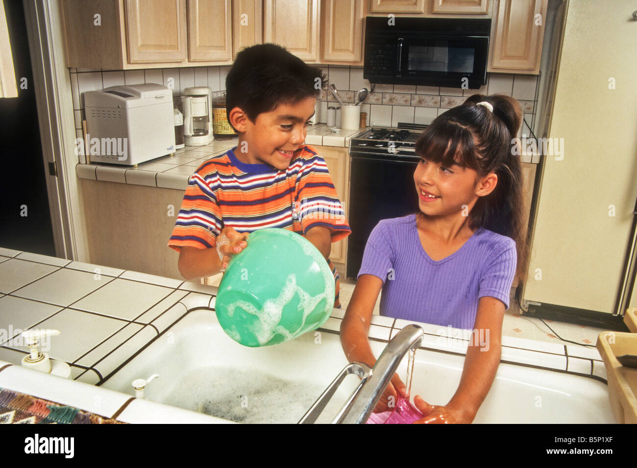 Hispanic twin boy and girl wash dishes in family kitchen Stock Photo ...