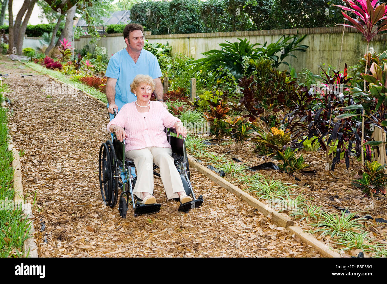 Nursing home orderly pushing a disabled senior woman through the garden ...