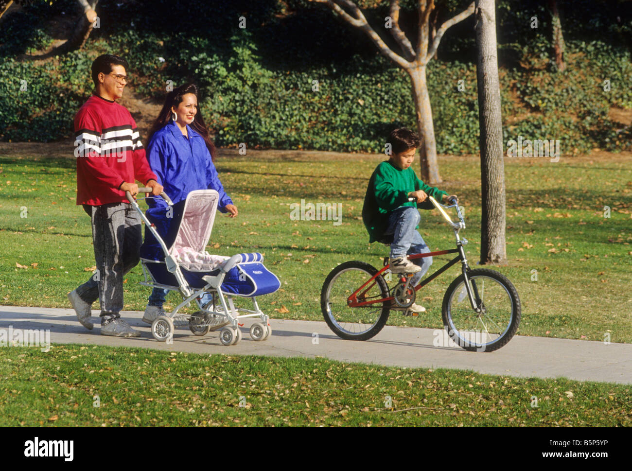 Hispanic husband and wife push stroller with baby while older brother ...