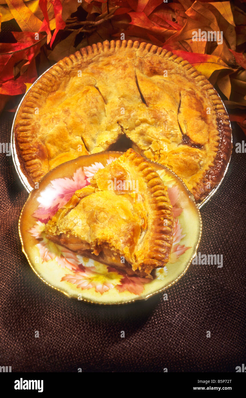 Apple pie slice on plate in front of rest of pie in pan Stock Photo - Alamy