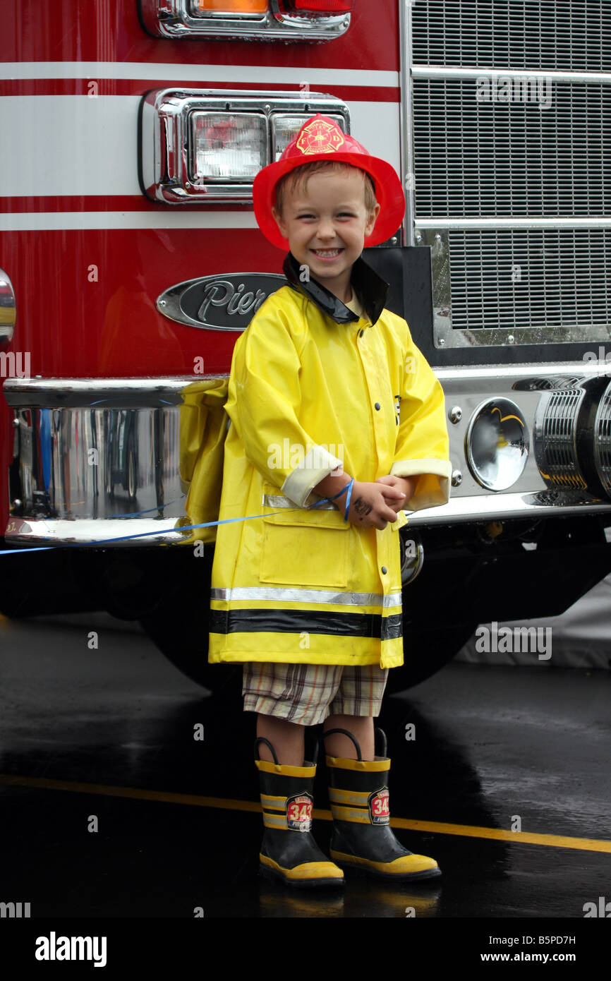 A little boy standing in front of a fire engine in a rain coat after it ...