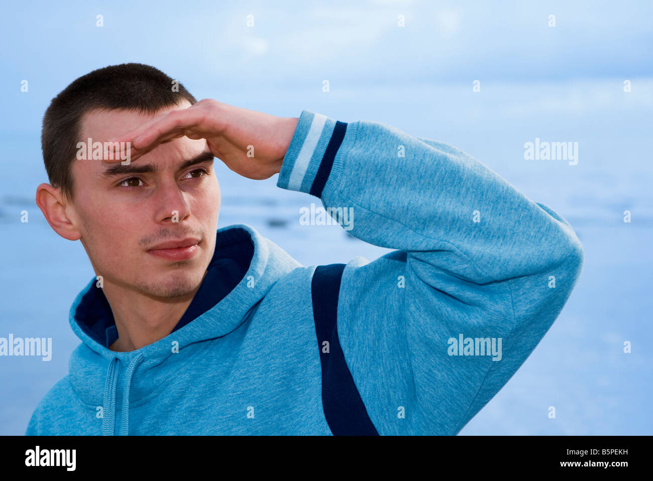 Young man looking to side shielding eyes from sun Stock Photo - Alamy