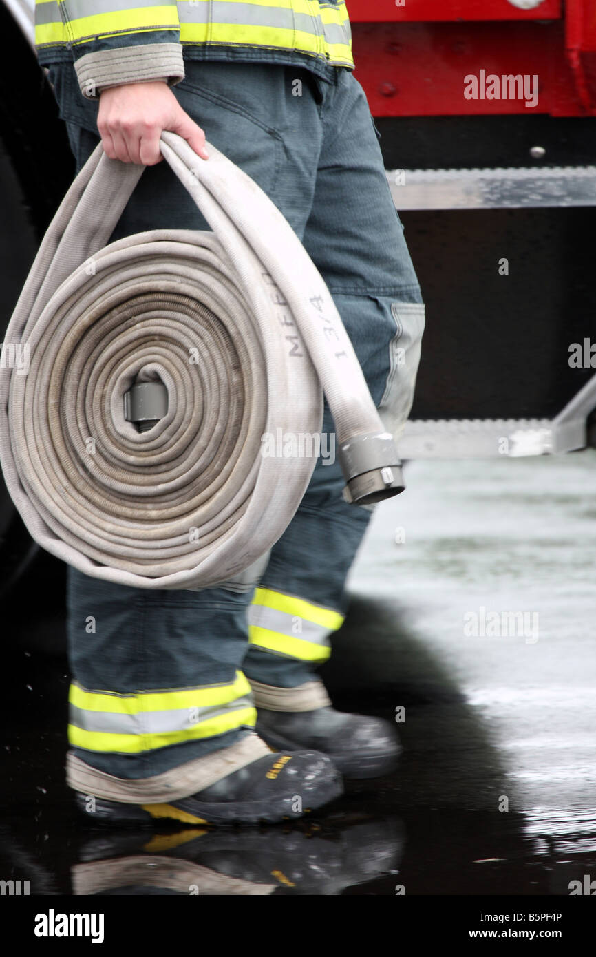 A firefighter carrying the hose of a fireline at a scene after it has ...