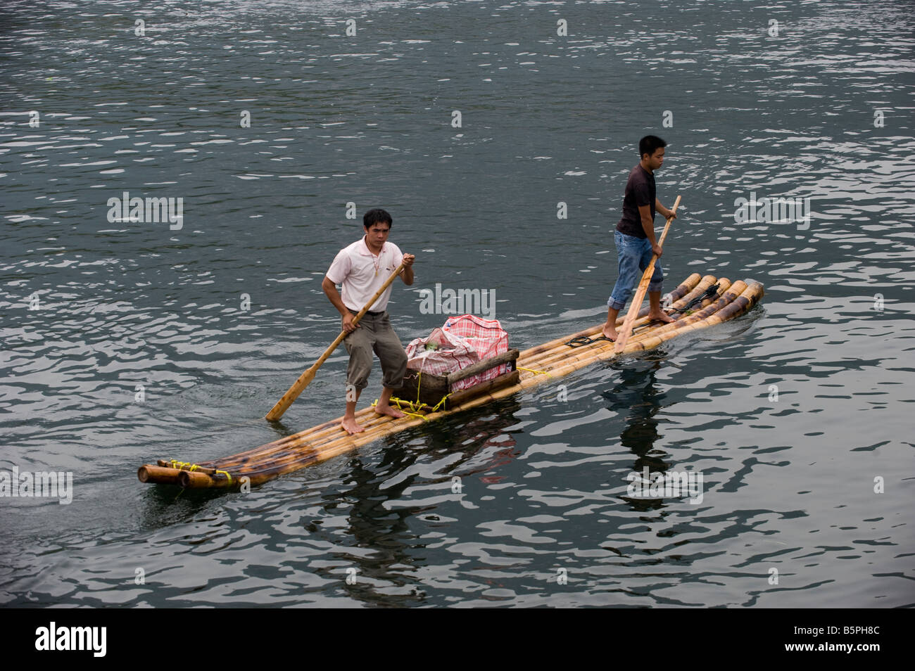 Chinese souvenir salesman paddling his bamboo raft looking for tourists ...