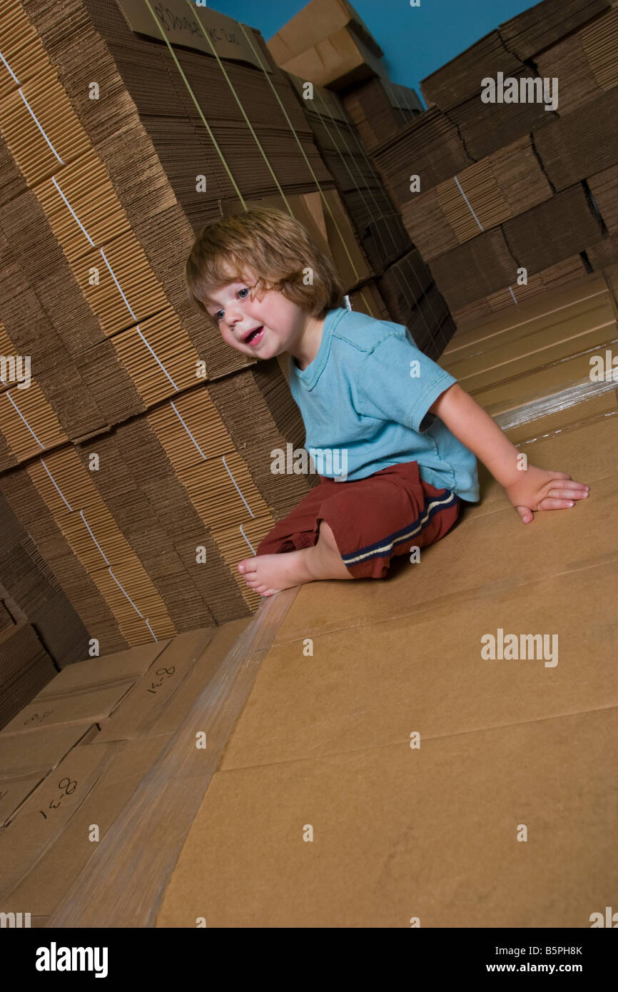 Young boy on a pile of cardboard boxes in a factory MODEL RELEASED ...