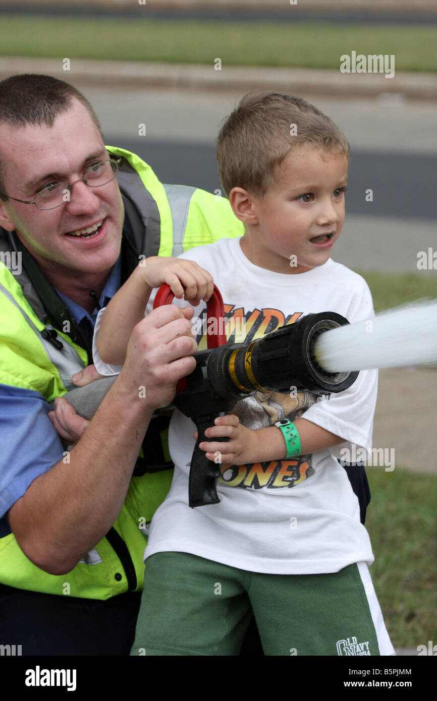 A firefighter helping a young boy use the fire hose to put out a ...