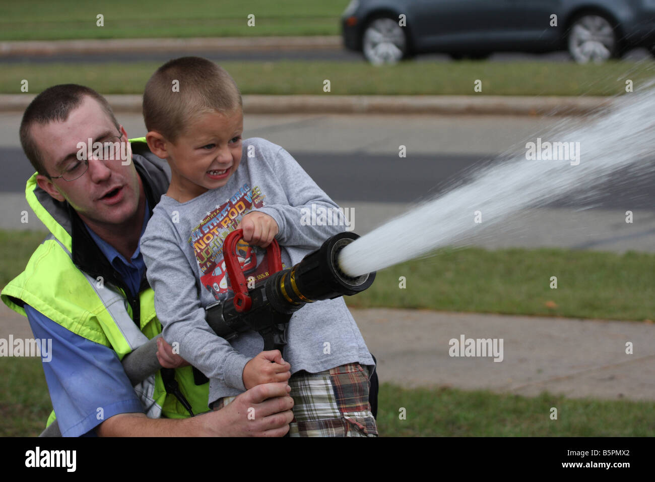 A firefighter helping a young boy use the fire hose with such ...