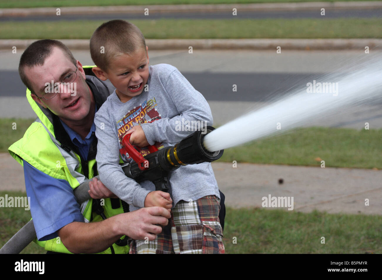 A firefighter helping a young boy use the fire hose with such ...