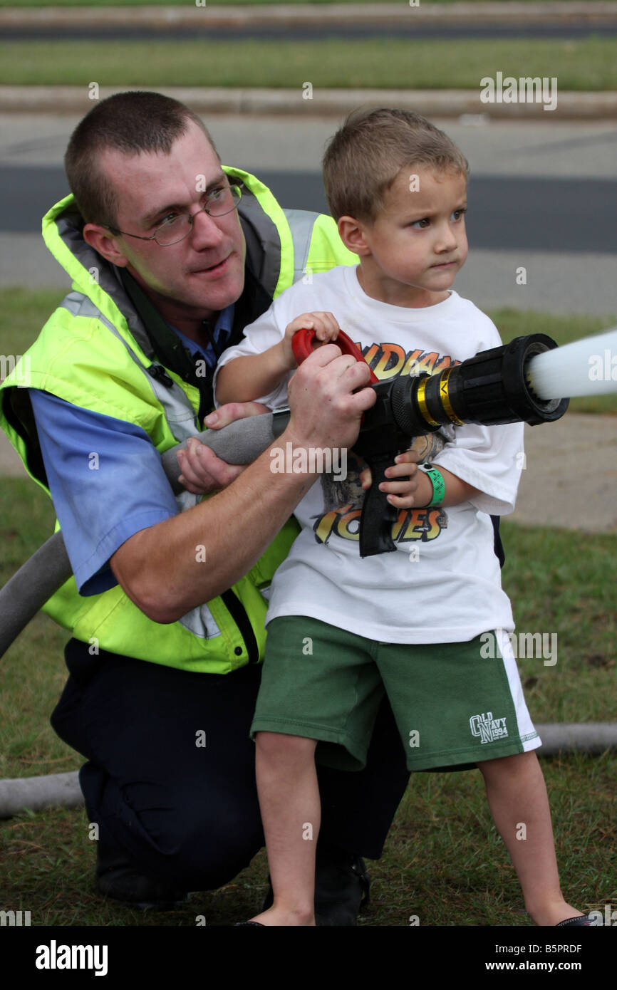 A firefighter helping a young boy use the fire hose to put out a ...
