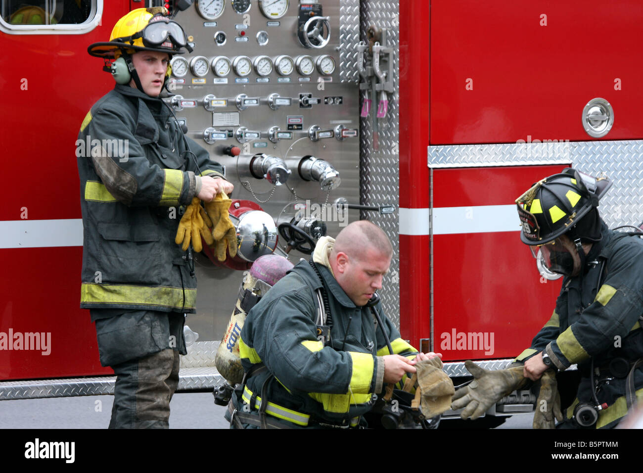 Three firefighters getting ready in front of a fire truck to fight a ...