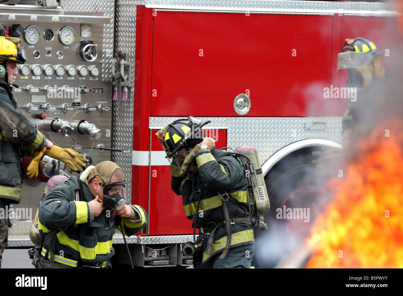 Four firefighters getting a hoseline ready from a fire truck at a fire ...