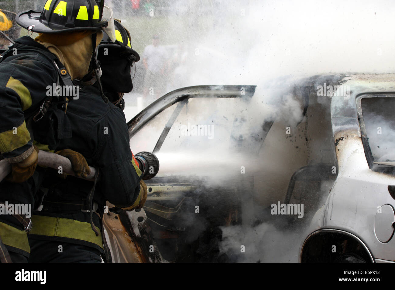 Three firefighters putting out a car fire surrounded by smoke water and ...