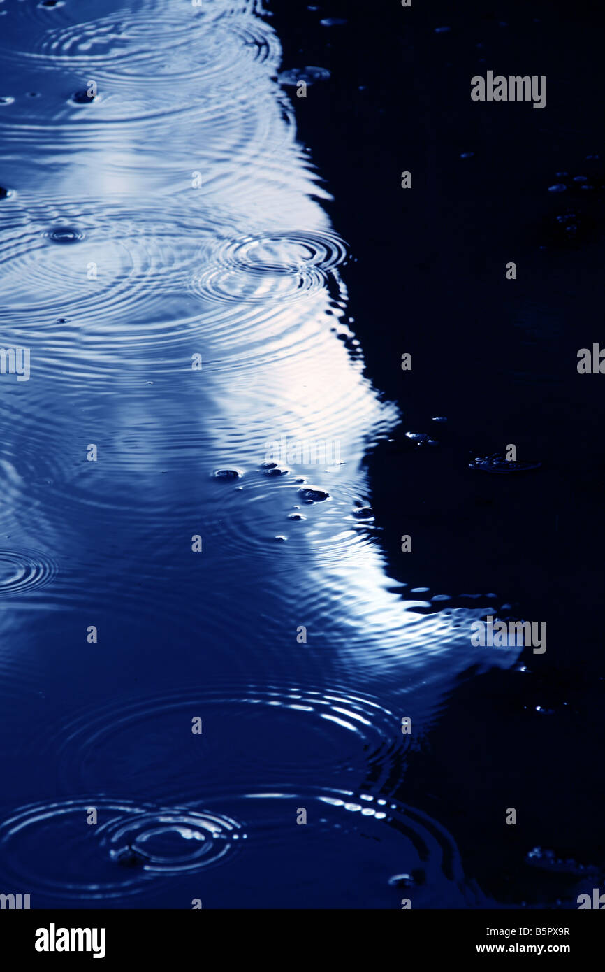 rain drops falling in cold blue water puddle in street at night Stock ...