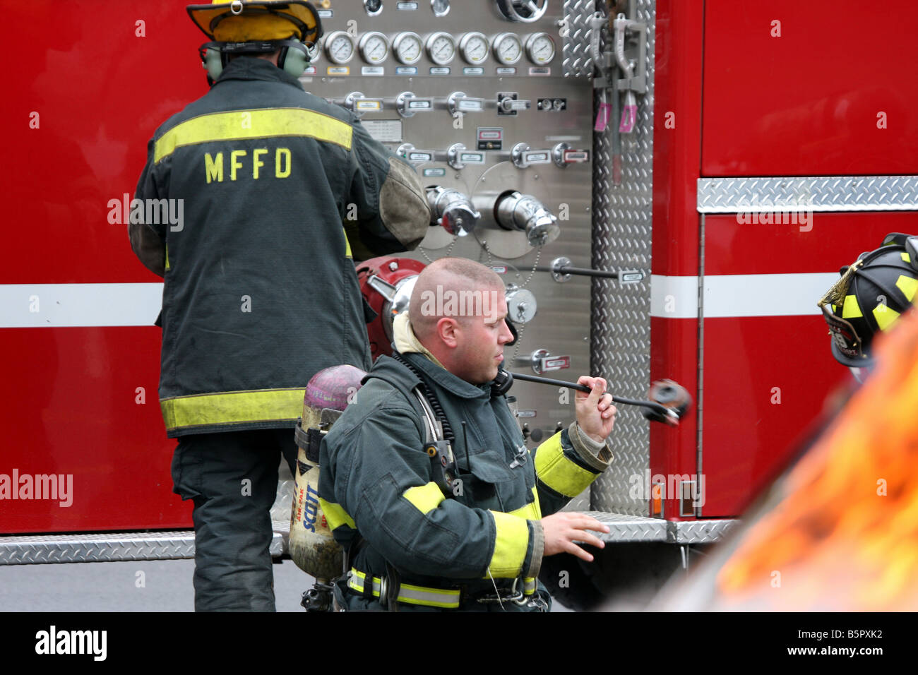 Three firefighters getting ready in front of a fire truck to fight a ...