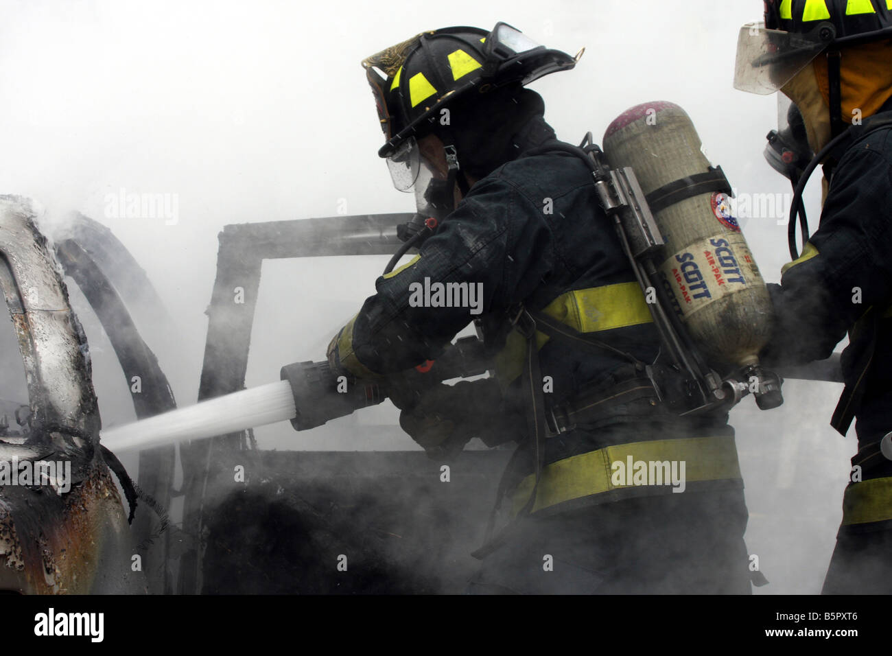 Two firefighters putting out a car fire surrounded by smoke water and ...