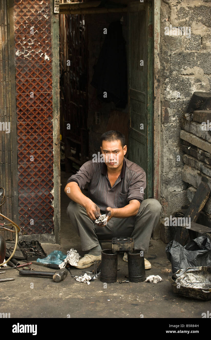 A Chinese man working metal seated in front of he shop in Yangshou, in ...