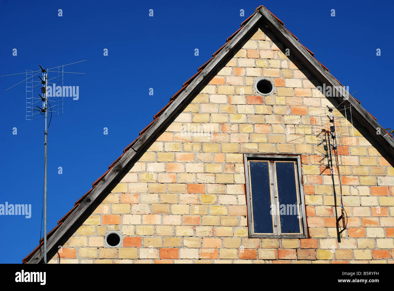 Three-cornered roof of village house with attic and antennas against ...