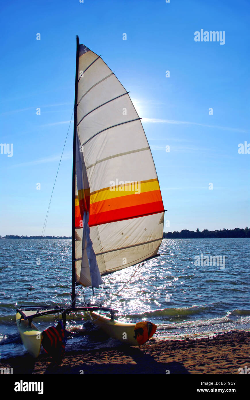 Catamaran on a beach with backlit sail Stock Photo - Alamy