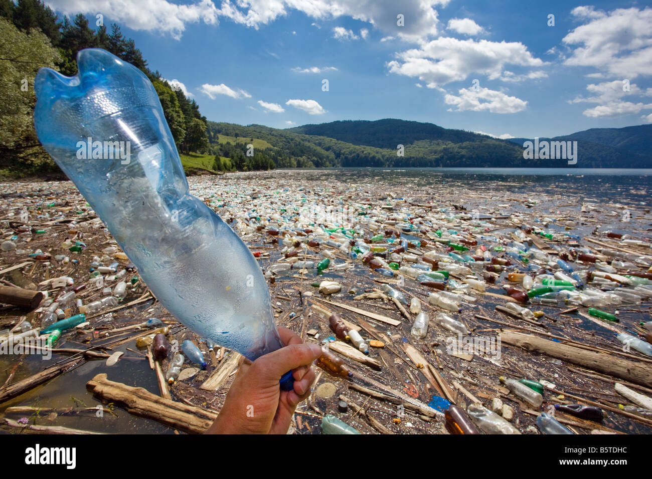 hand throwing plastic bottle in beautiful landscape ruined by pollution ...