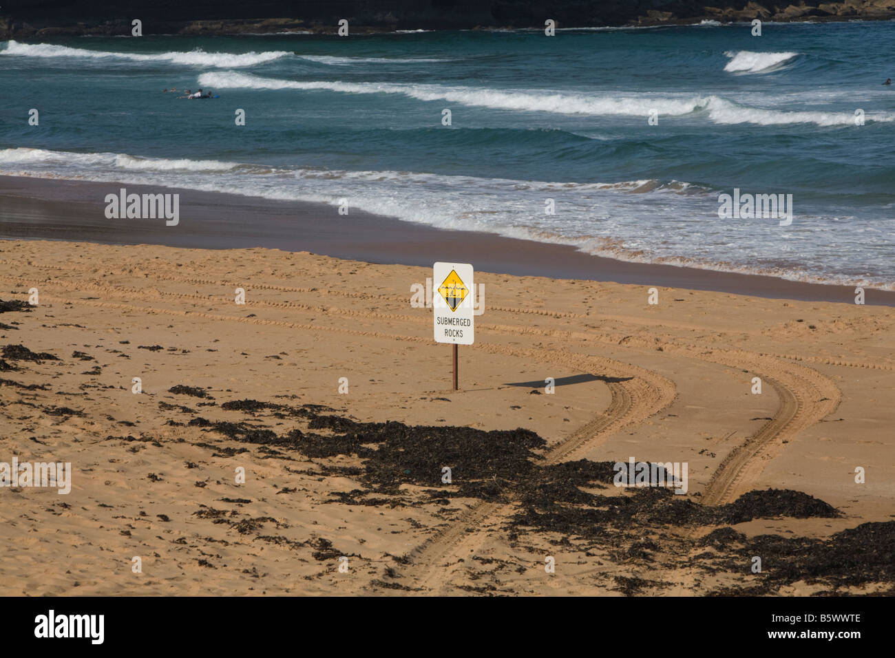 submerged rocks warning sign on bilgola beach alongside tyre tracks in ...