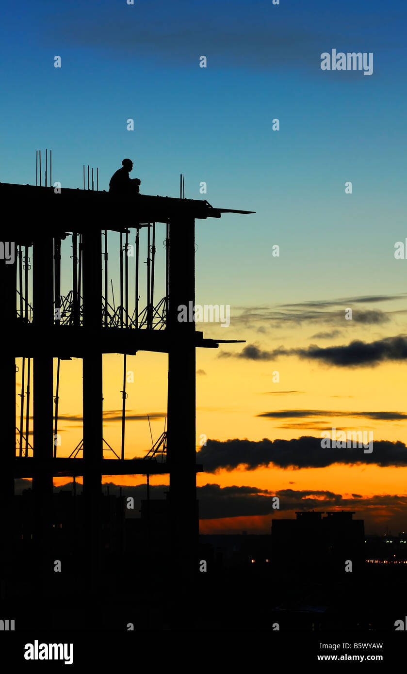 Lonely construction worker sitting at the edge of unfinished house ...