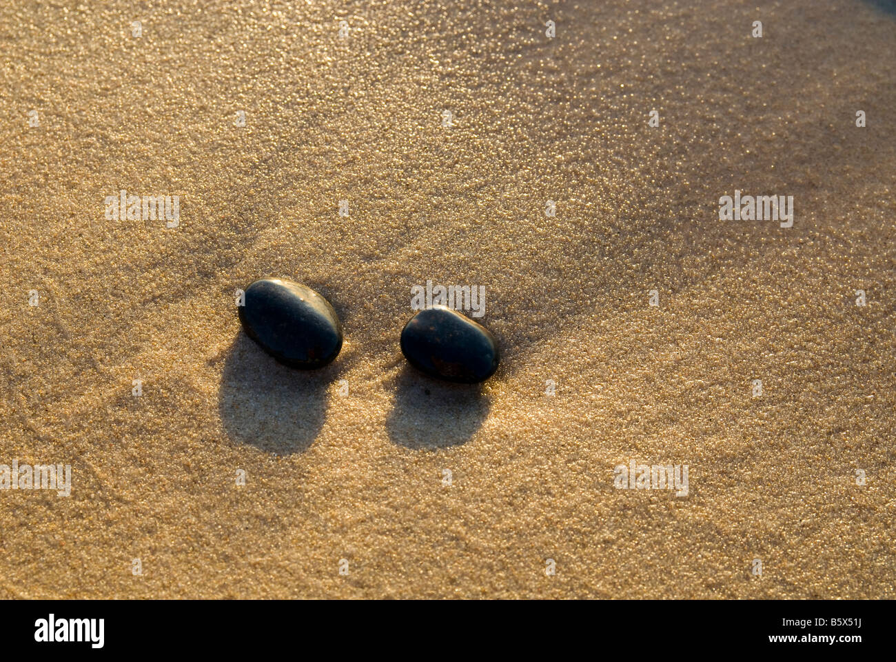 Two black stones in white sand Stock Photo - Alamy