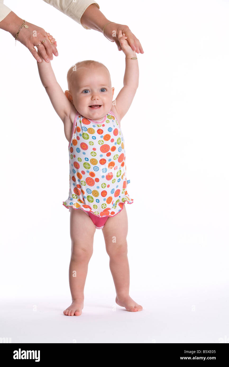 Baby girl standing with help of parents hands Stock Photo - Alamy