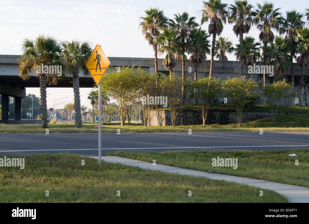 Yellow pedestrian crossing sign pointing across a highway by a bridge ...