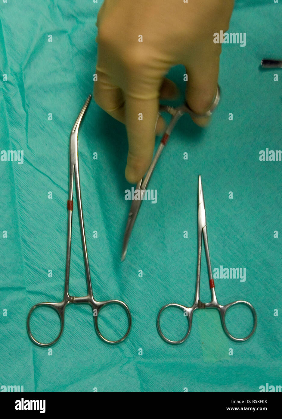 A surgeon picks up forcep surgical instruments from a table in an NHS ...