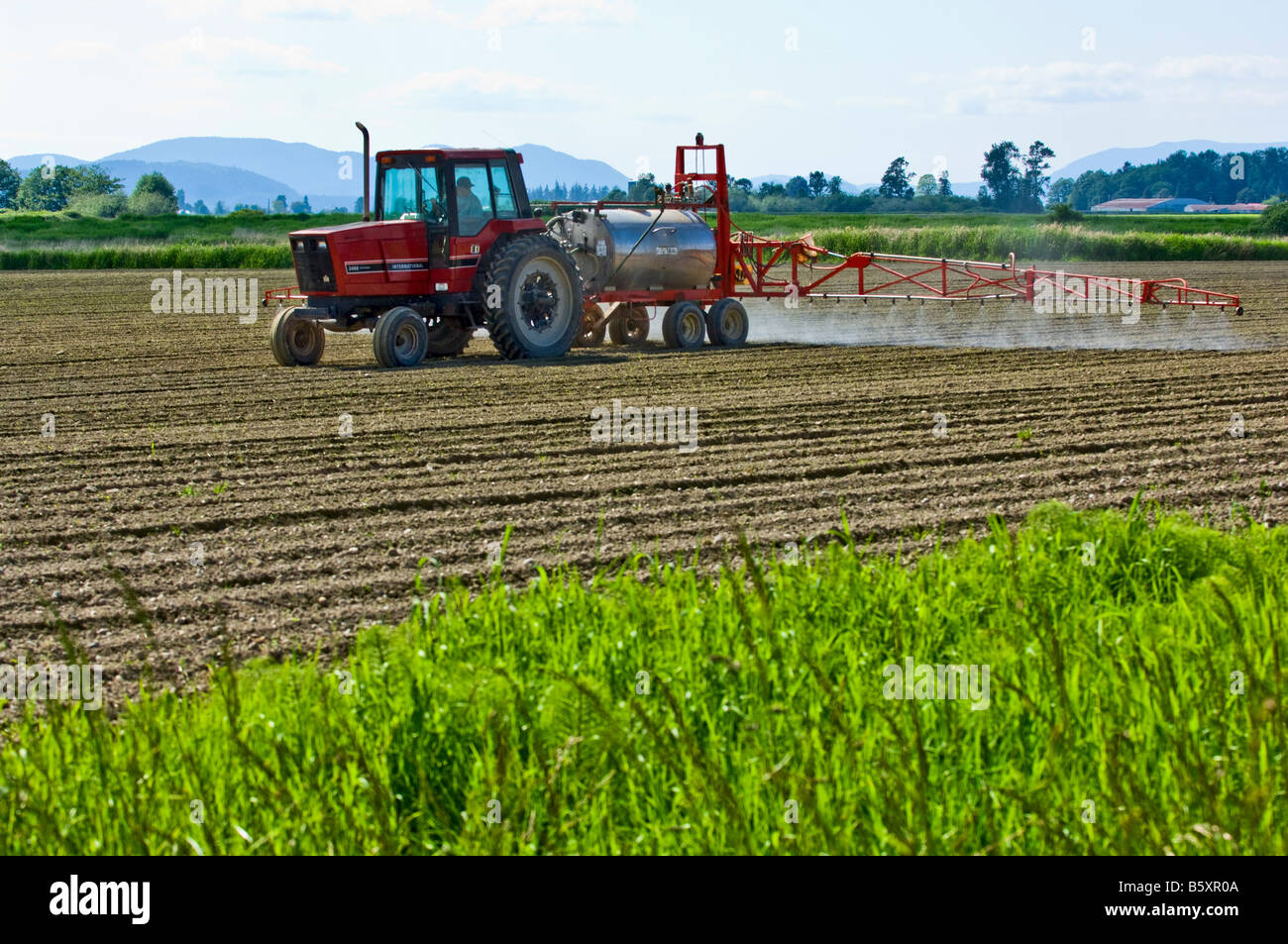 A tractor pulling a spray rig sprays a freshly planted potato field to ...