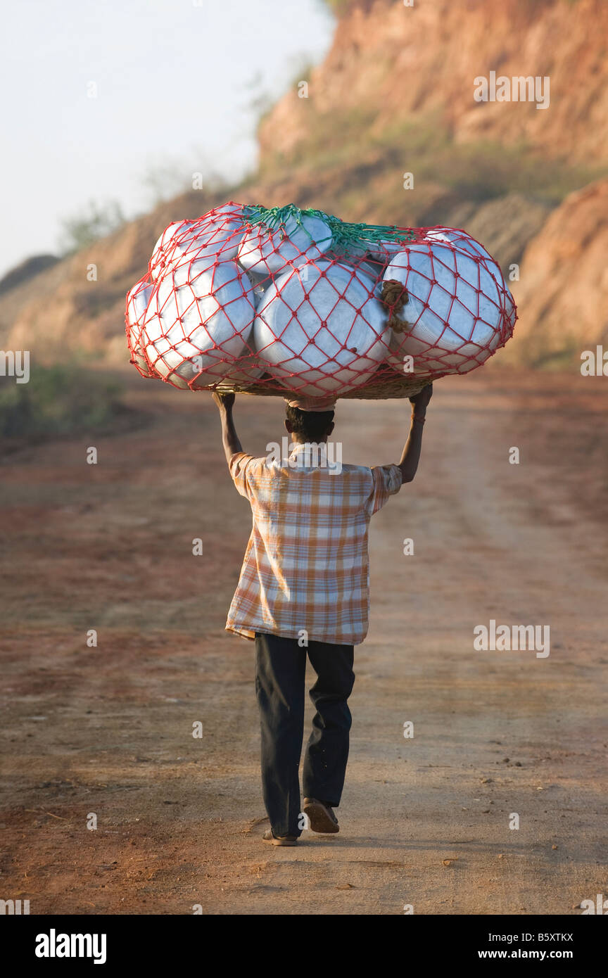 Indian man carrying metal cooking pots on his head in netting. Andhra ...