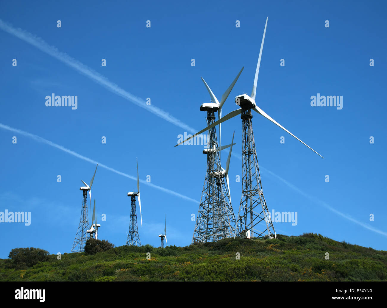 Modern windmills turbine on green ground against blue sky with white ...