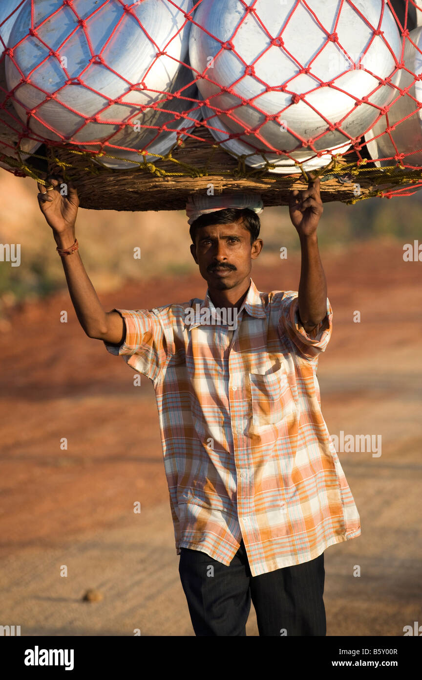 Indian man carrying metal cooking pots on his head in netting. Andhra ...