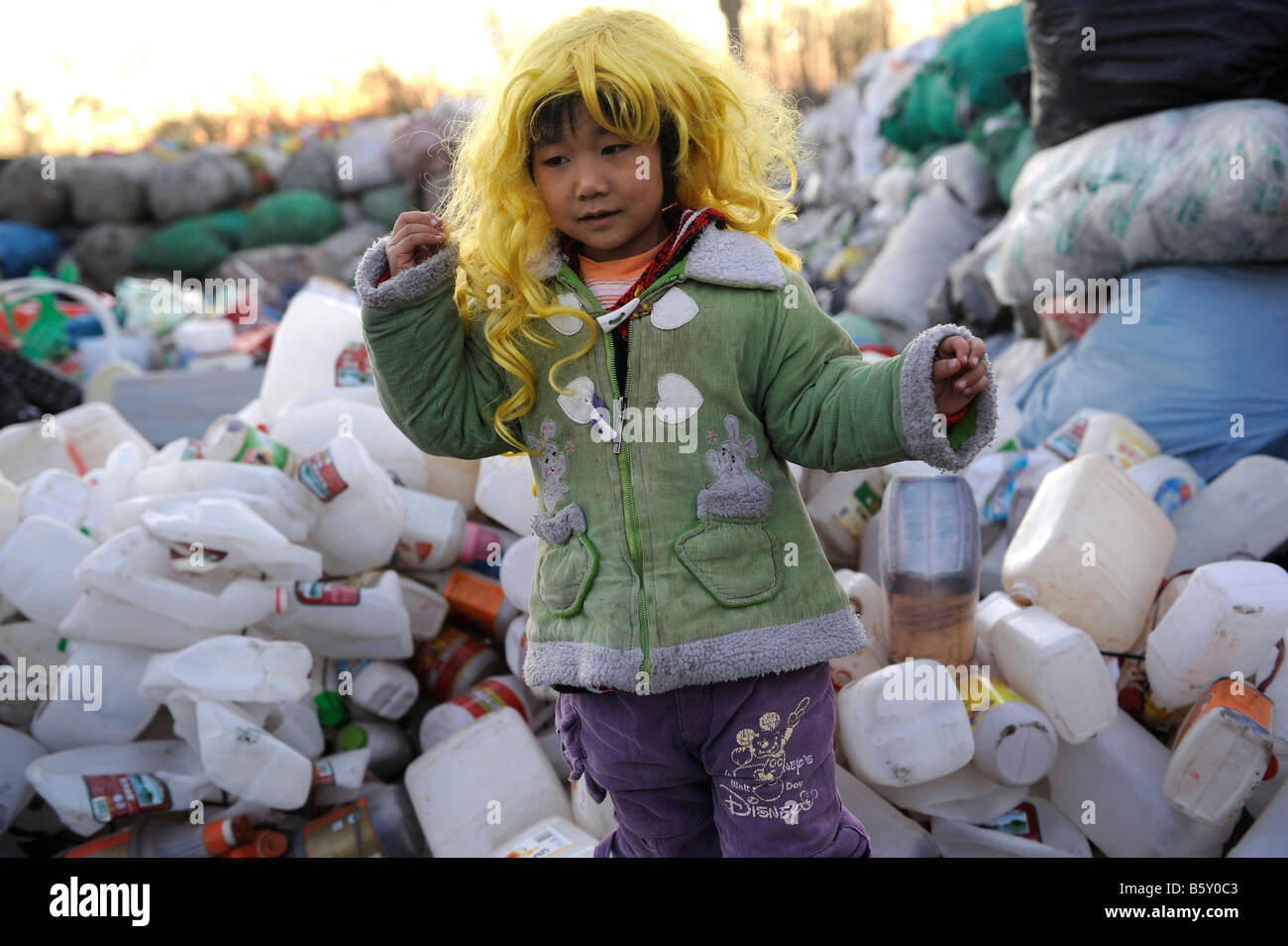 A little girl wearing a wig collected from trash at a recycling station ...