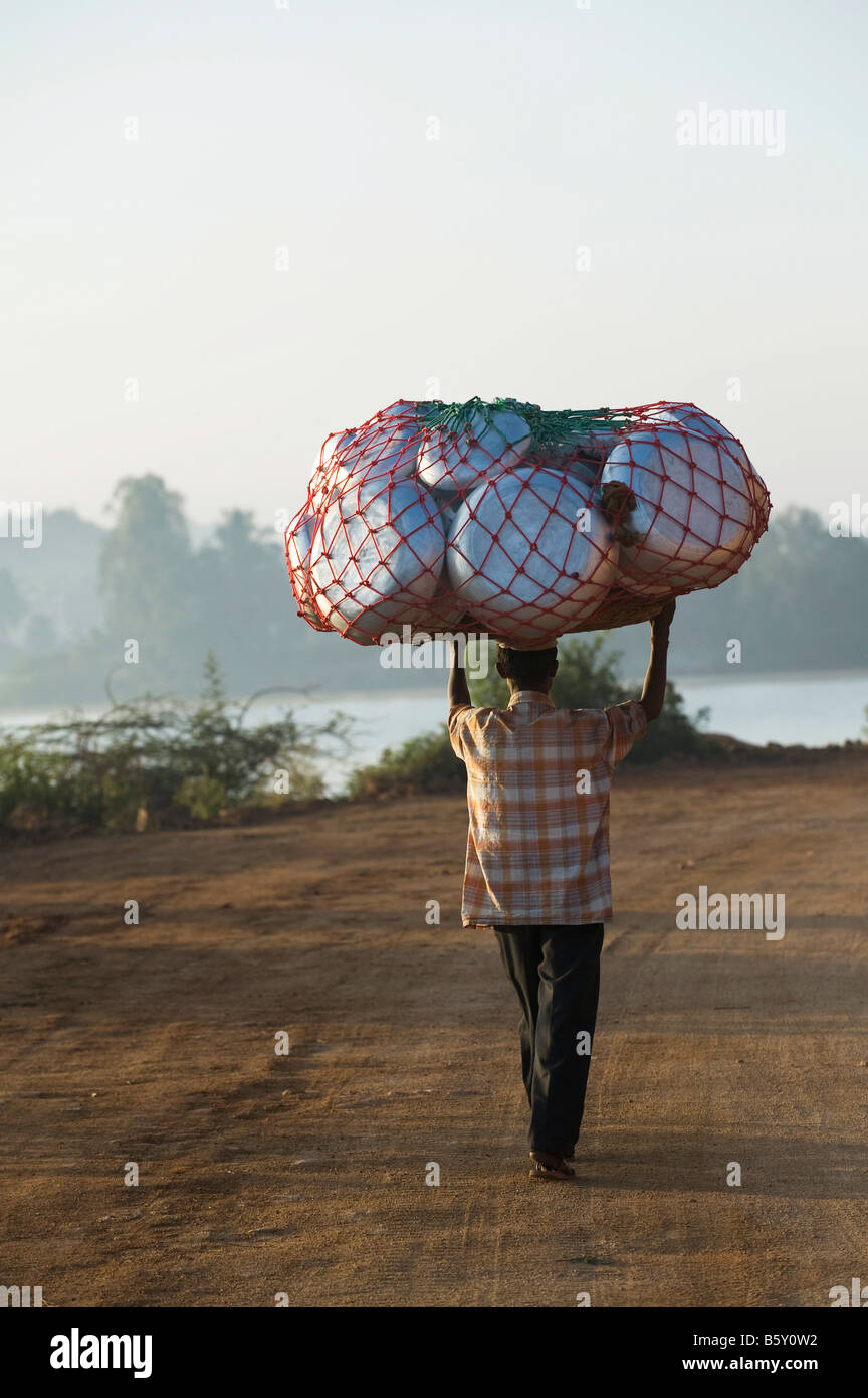 Indian man carrying metal cooking pots on his head in netting. Andhra ...