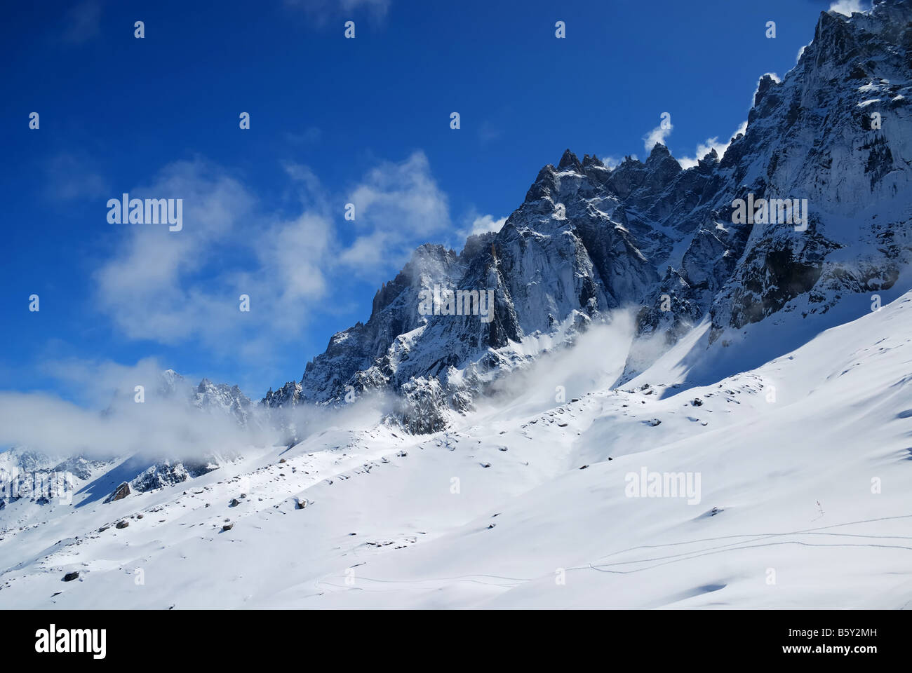 Steep peaks in light clouds and snow slopes against blue sky the Alps ...