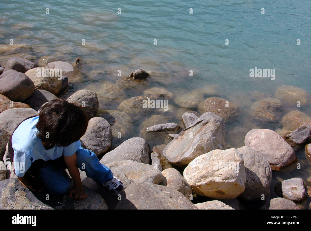 Young boy sitting on rocks near the shore Stock Photo - Alamy