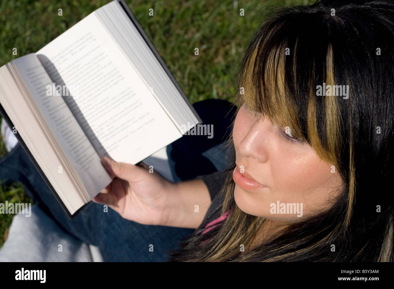 A young woman with highlighted hair reading a book or doing homework on ...