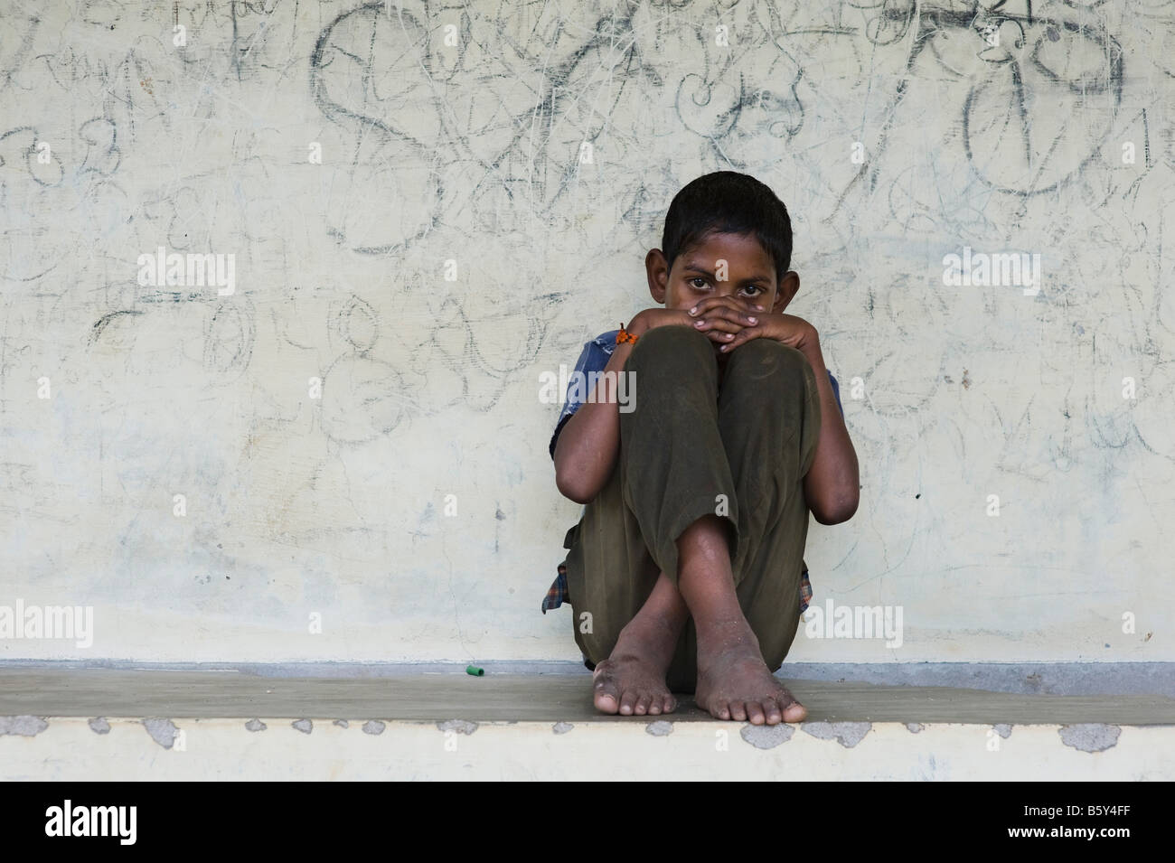 Sad Indian boy sitting against a wall covered in graffiti Stock Photo ...