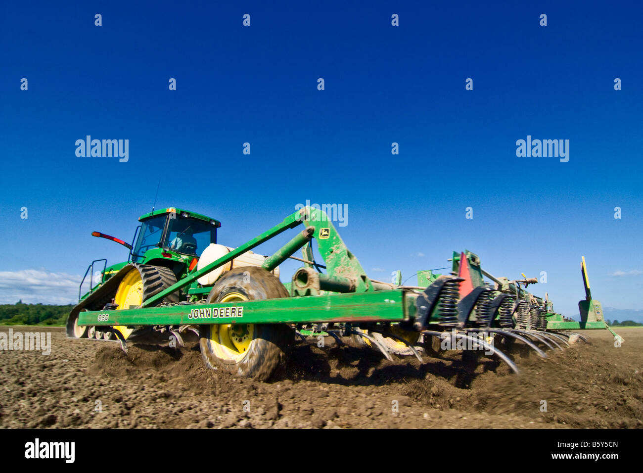 Tractor pulling a cultivator helps prepare a seedbed prior to planting ...