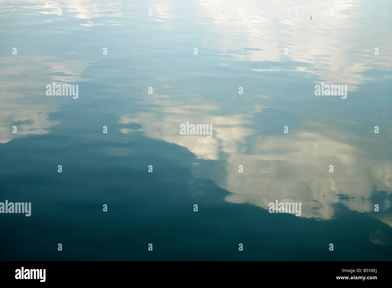 White clouds and blue sky reflected in a lake or river with ripples on ...