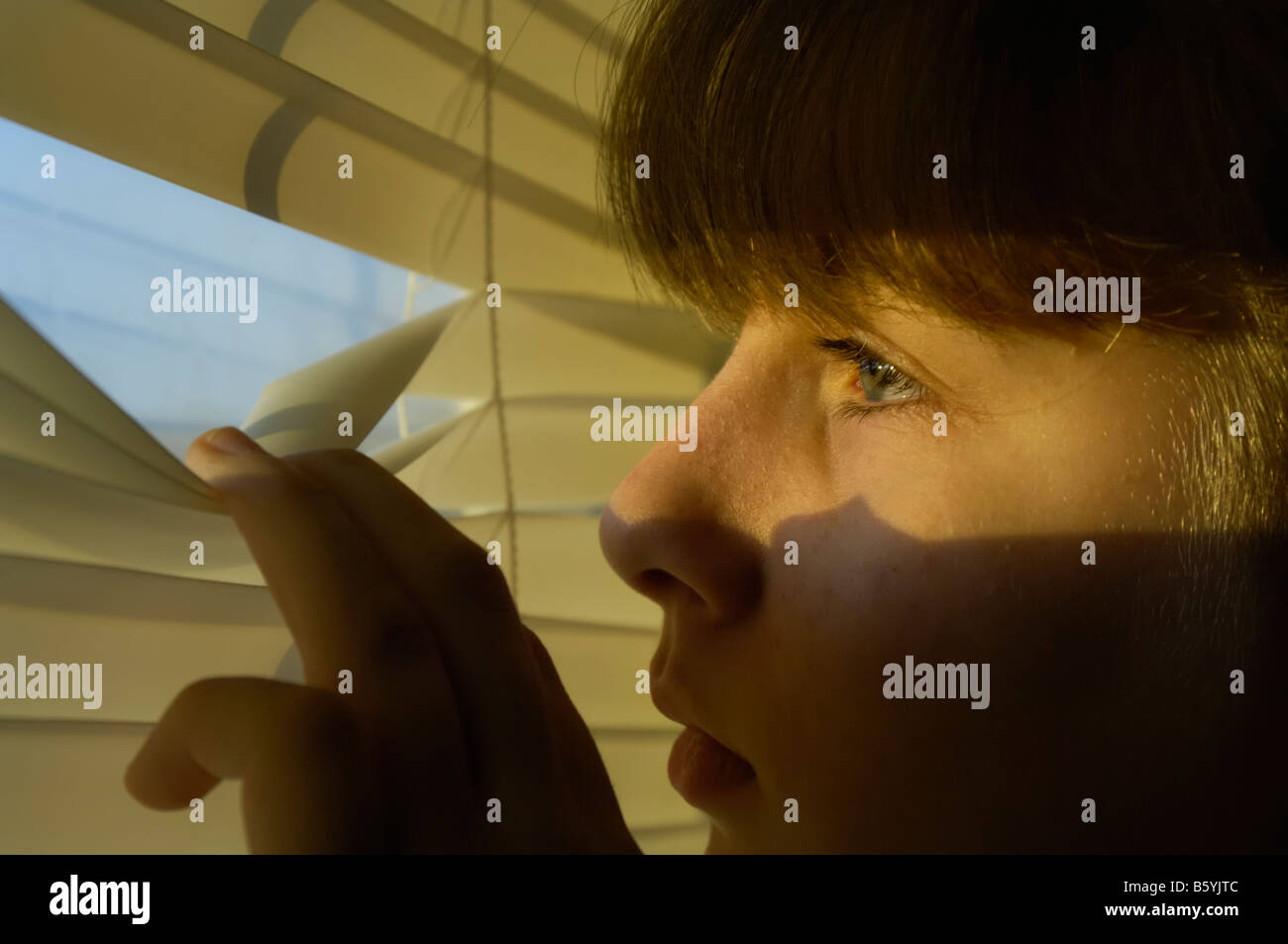Sad and depressed teen girl looks outside her window, into the sunshine ...