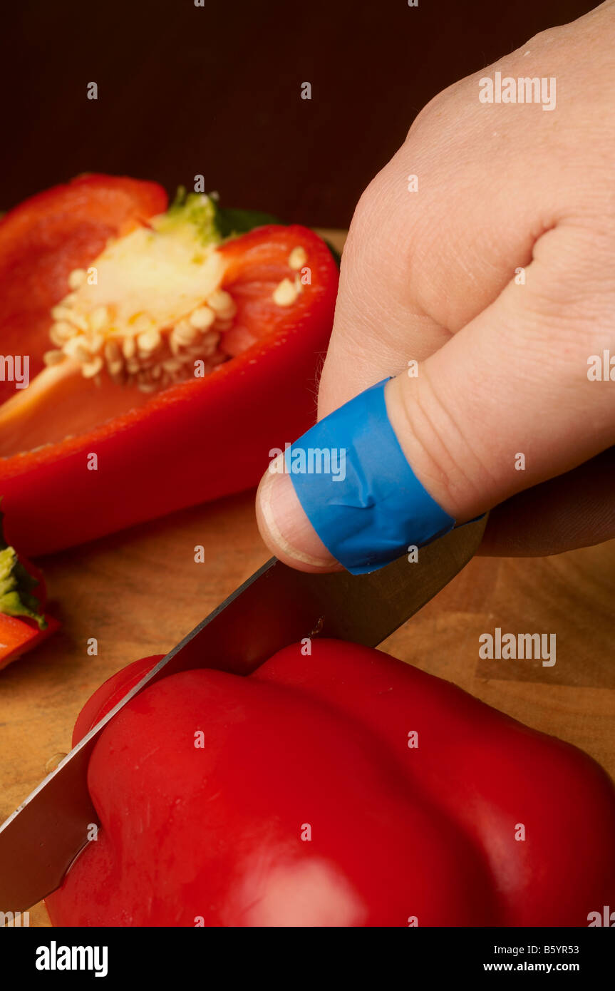 Man cutting red pepper with blue high visibility sticking plaster on ...
