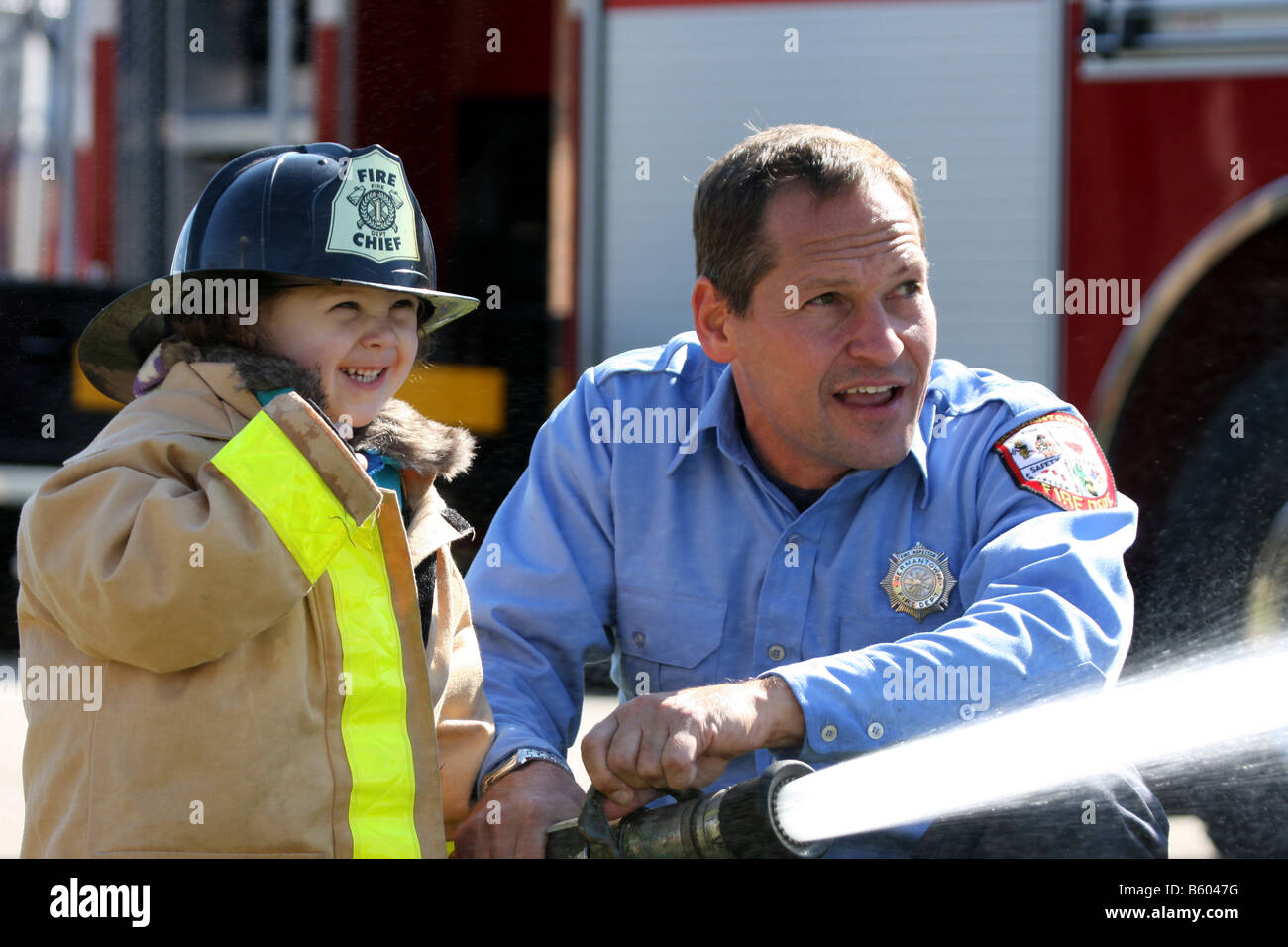 A firefighter showing a little girl how to use the hose line to fight ...