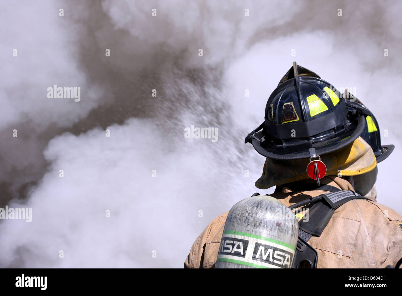 Three firefighters fighting a fire scene with smoke water spray and ...