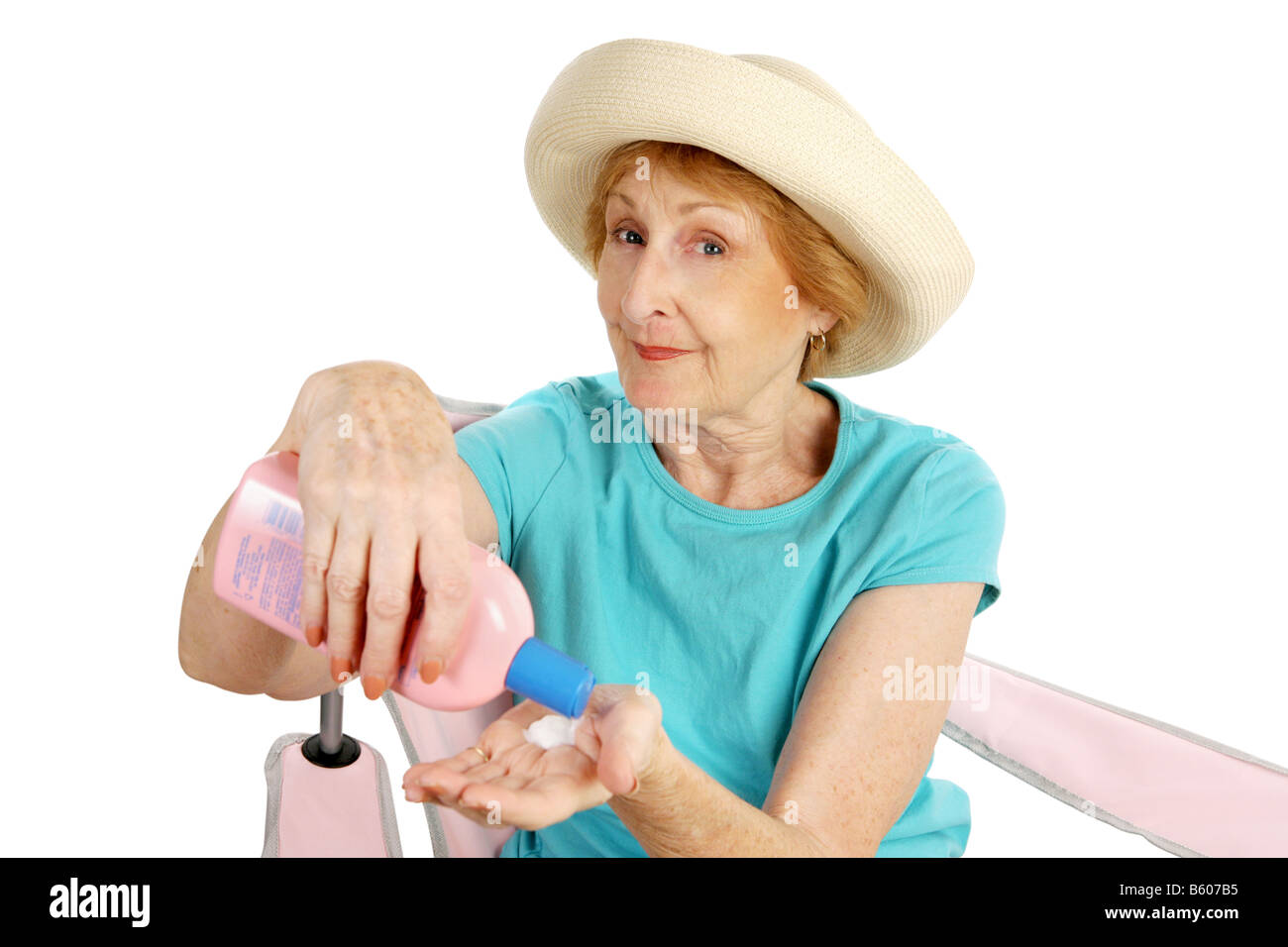 A fair skinned red haired senior lady applying sunscreen at the beach ...